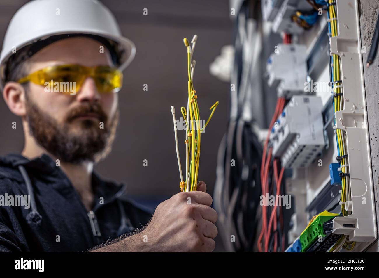 A male electrician works in a switchboard with an electrical connecting ...