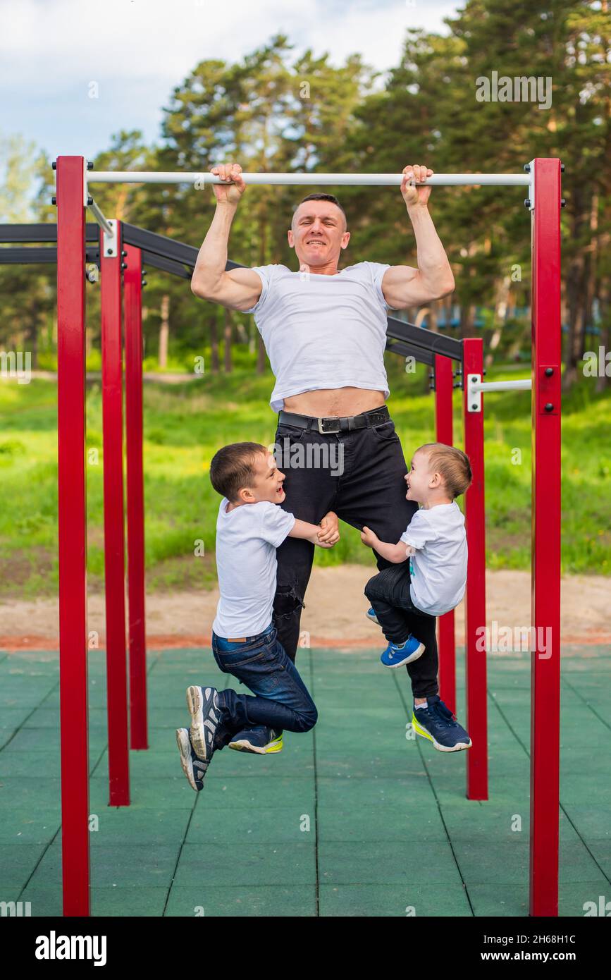 Caucasian man and two boys doing exercises outdoors. The father pulls ...