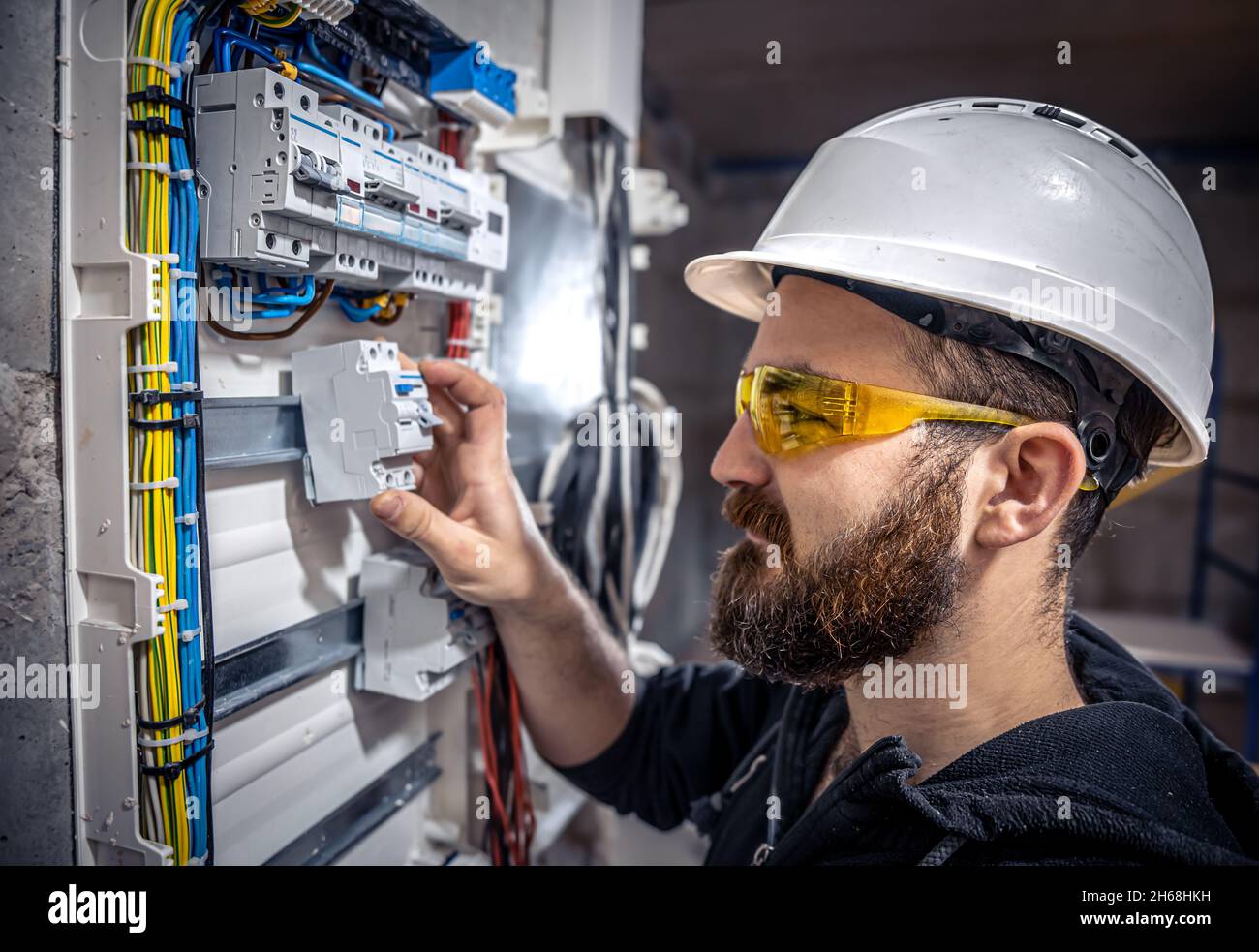 A male electrician works in a switchboard with an electrical connecting ...