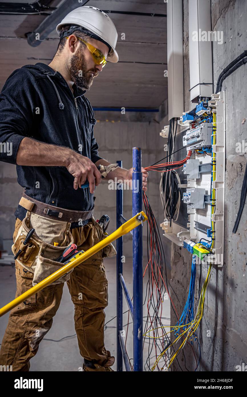 A male electrician works in a switchboard with an electrical connecting ...