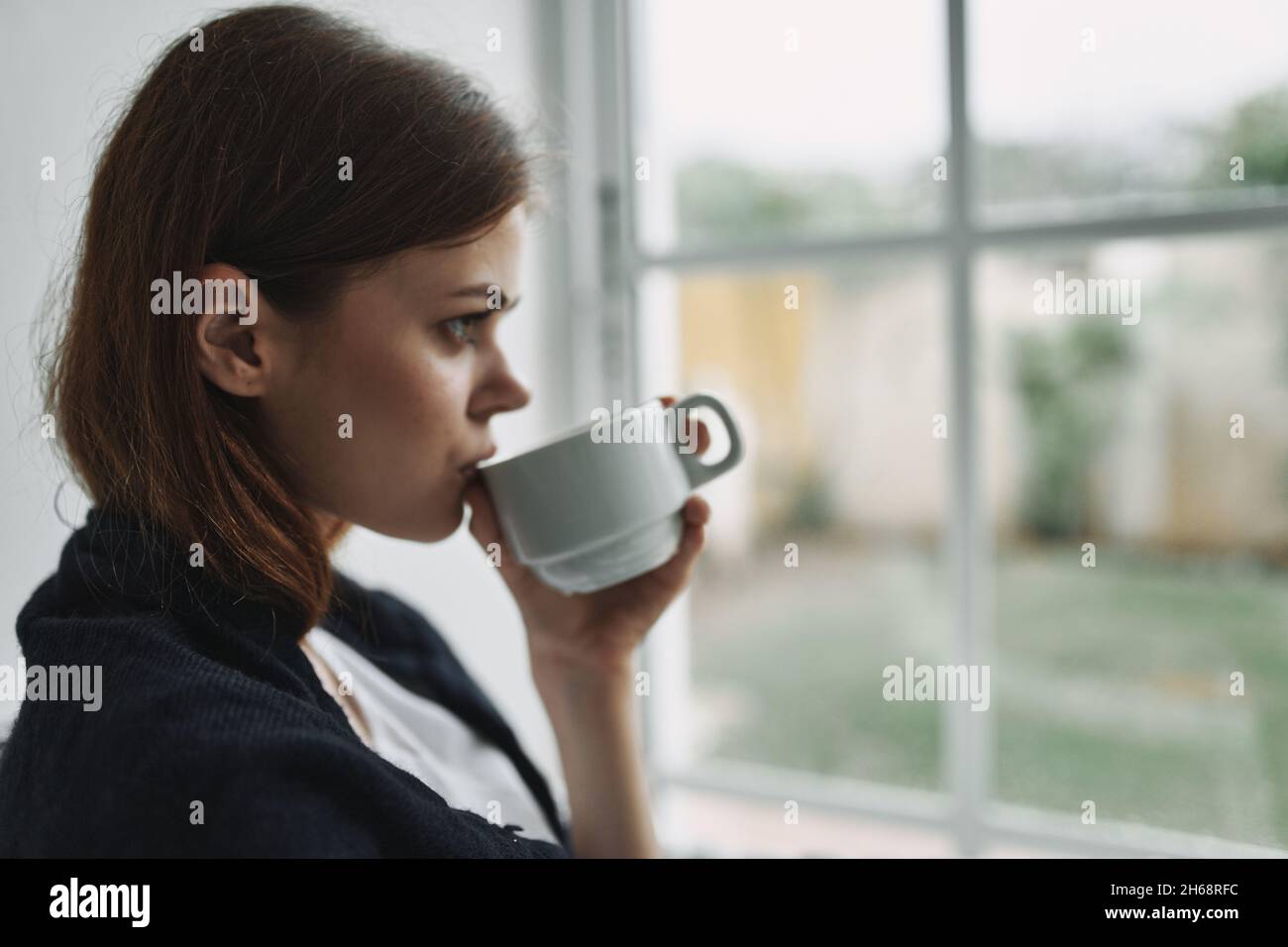 woman with a cup of tea in hand near the window portrait side view ...