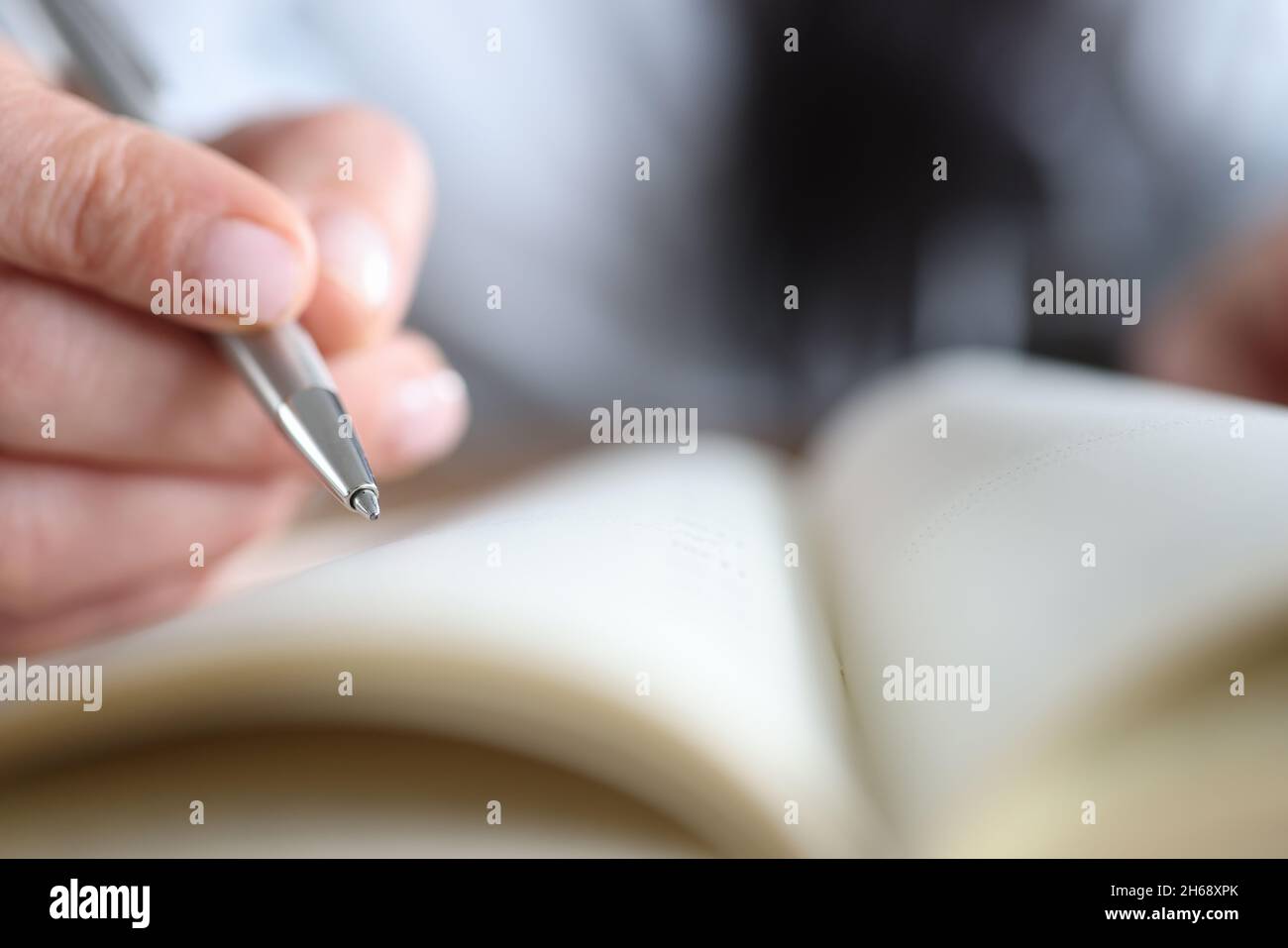 A woman's hand holds a pen near a notepad close-up, blurry. Document ...