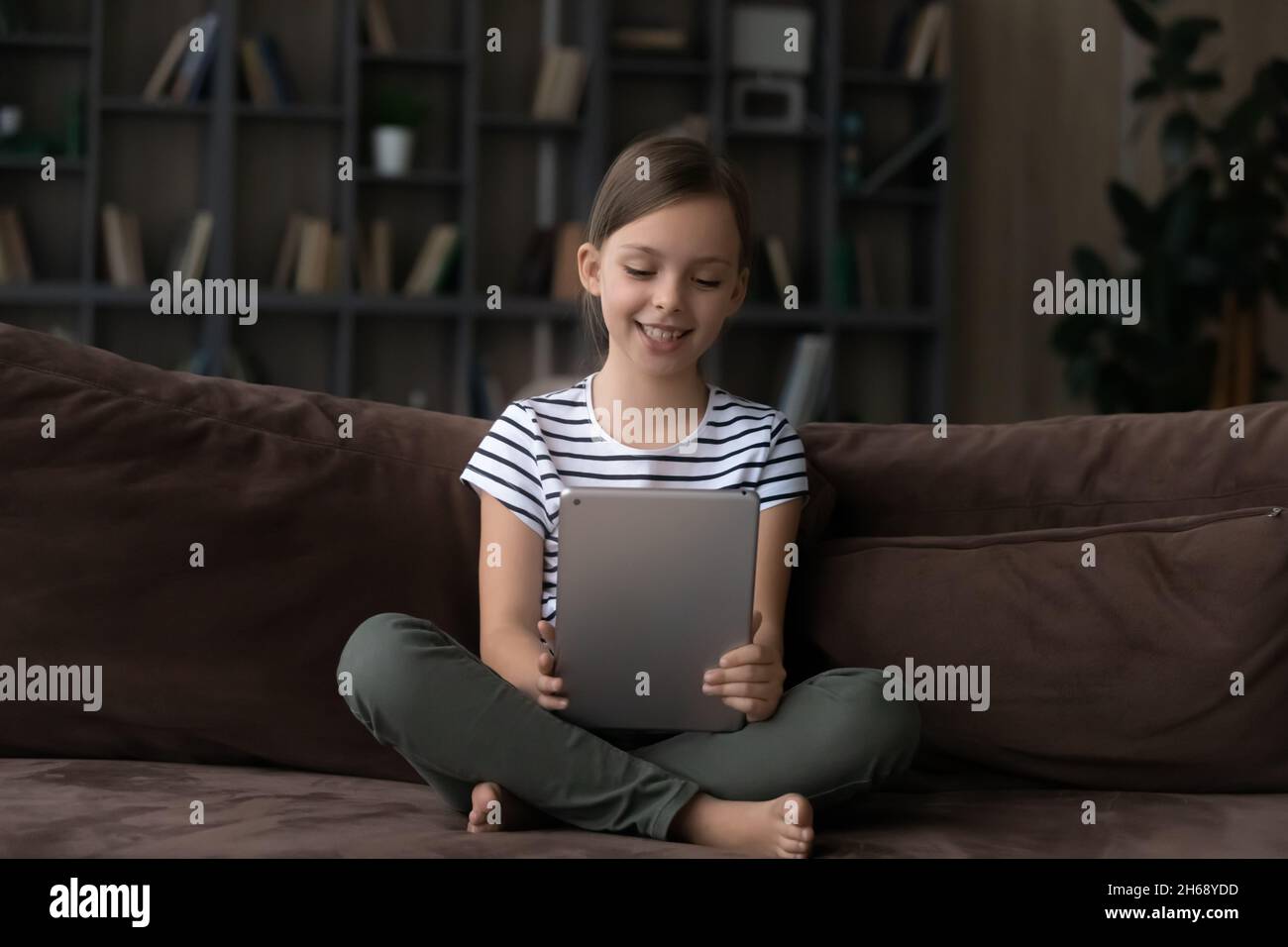 Happy cute girl kid using computer tablet, sitting on couch Stock Photo ...