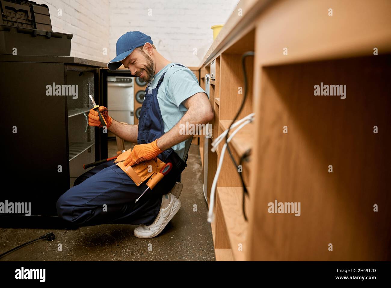Cheerful young man fixing fridge in kitchen Stock Photo - Alamy