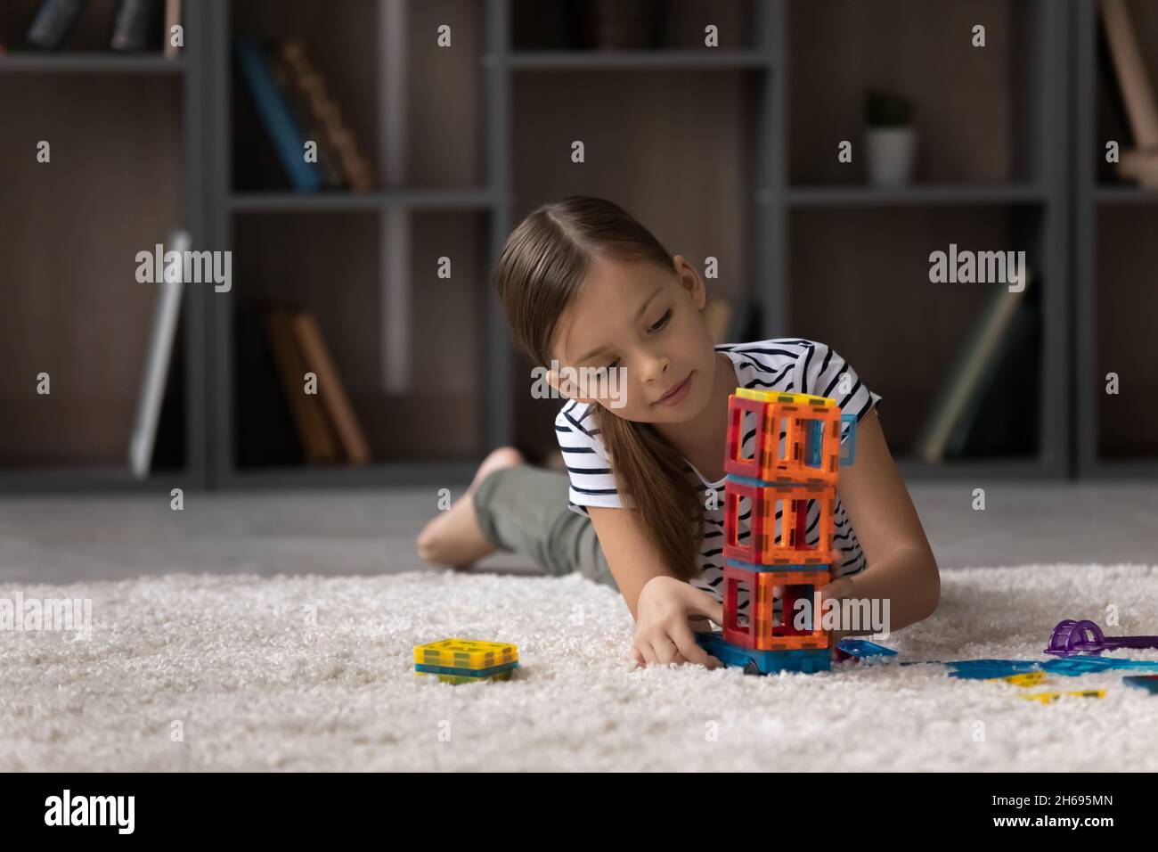 Little girl playing with colorful plastic blocks alone, building tower ...