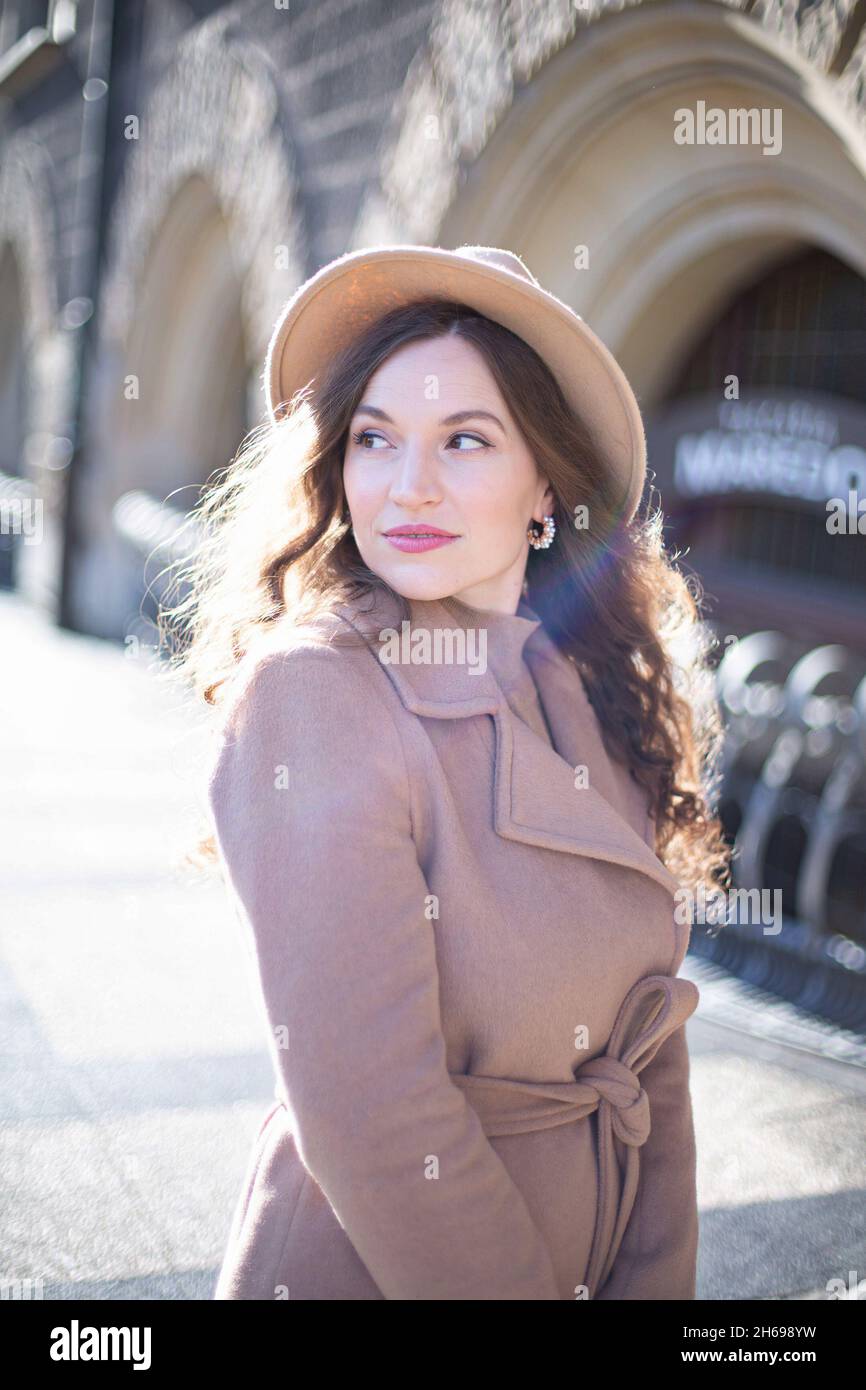 Portrait of pretty woman with curly hair in pastel pink coat with arch ...