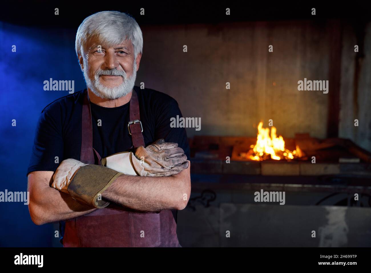 Caucasian blacksmith with grey hair and beard holding arms crossed near ...