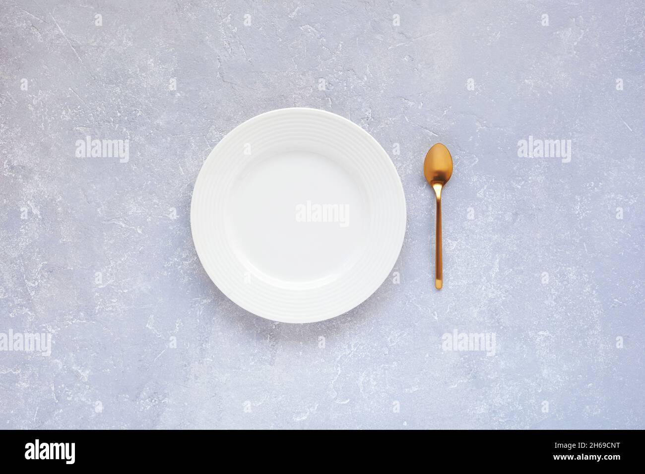 empty white dessert plate with a golden spoon in the middle of the grey ...