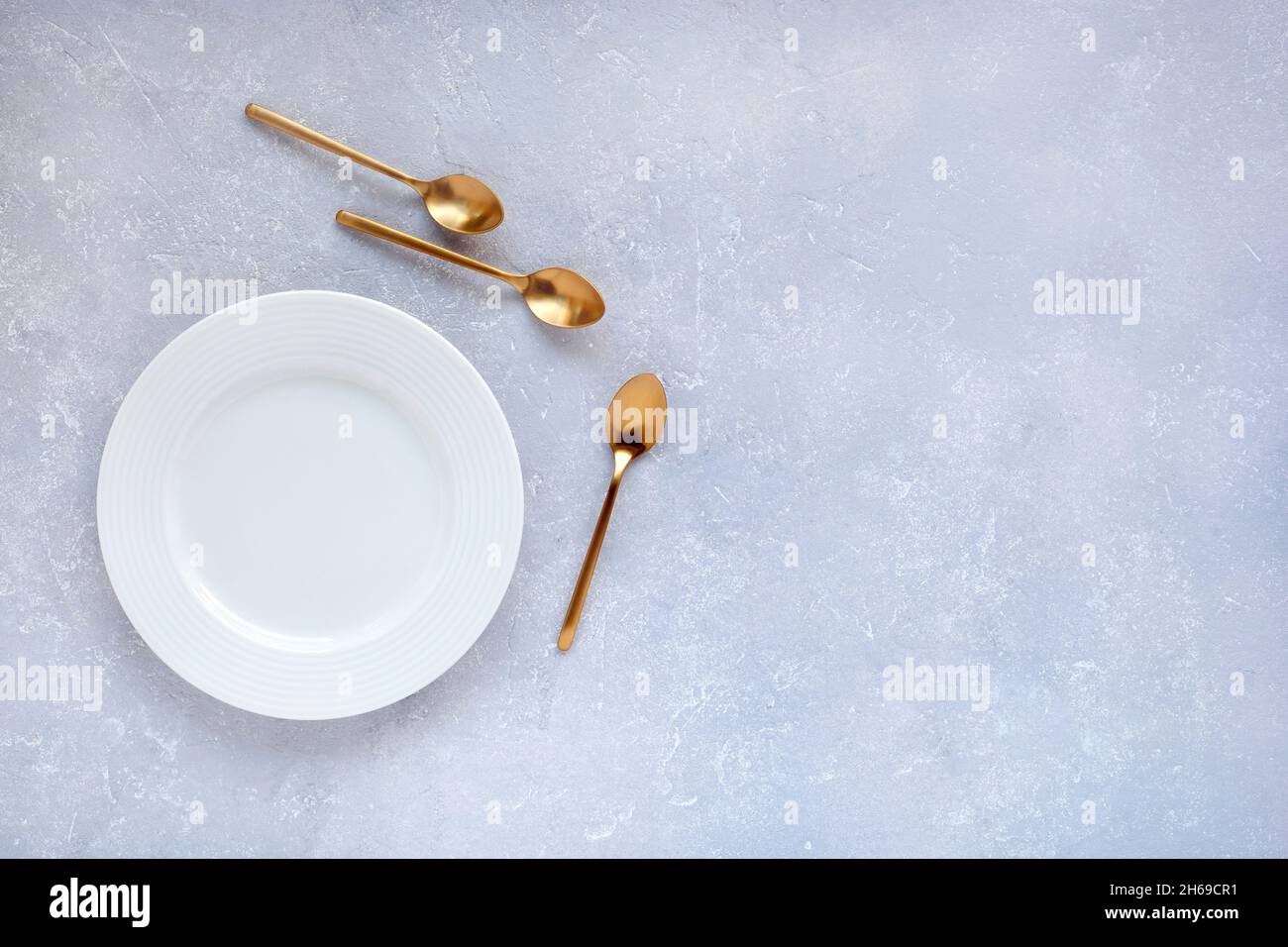 three golden dessert spoons near an empty plate on the grey background ...