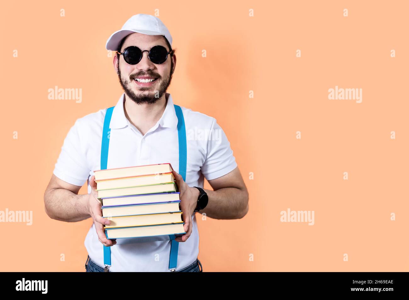 A book lover. Young man holding a stack of books on a light orange ...