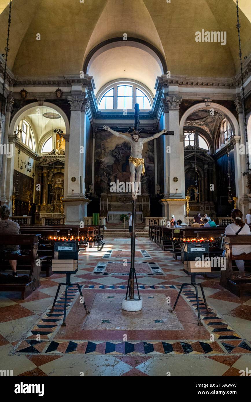 Crucifix in a church with worshippers sitting and praying on bench ...