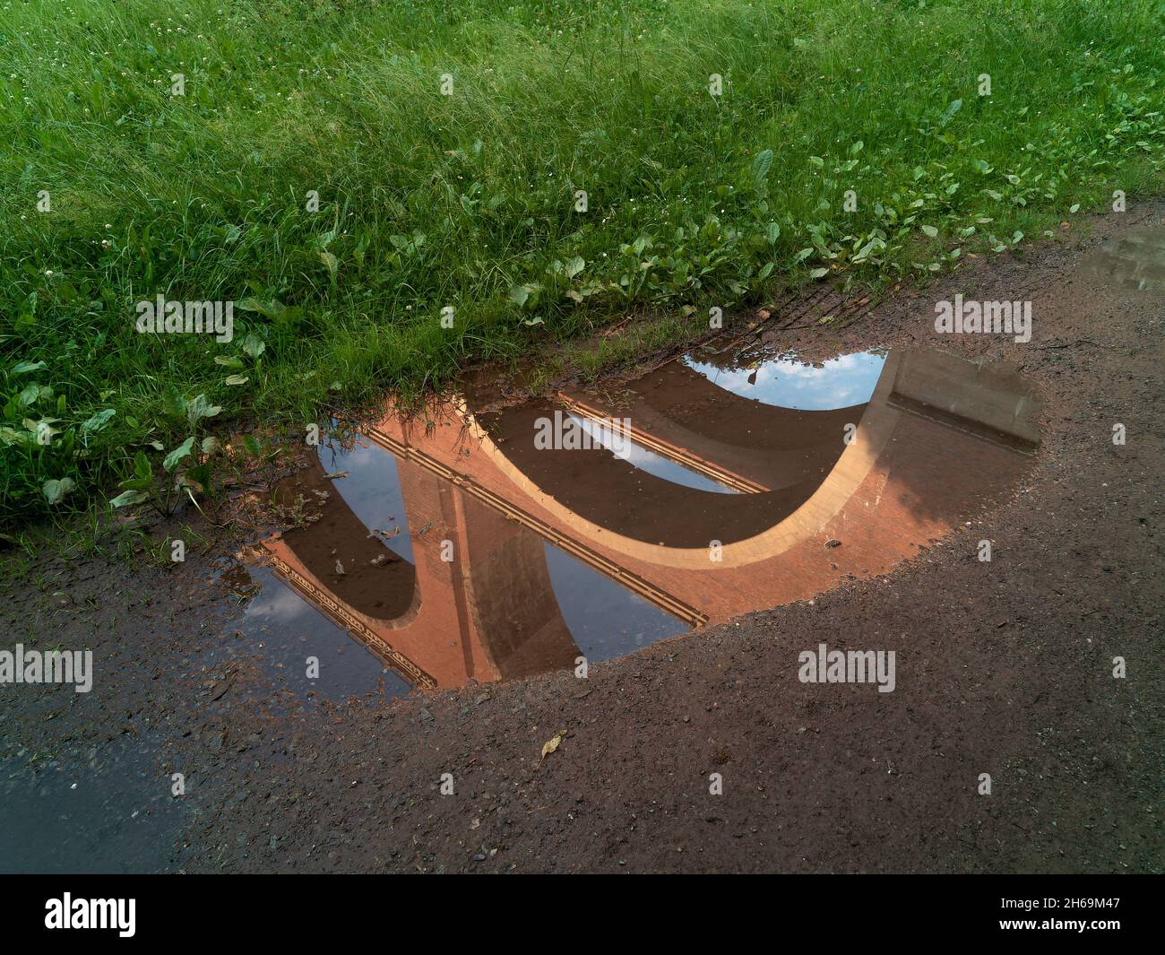 A puddle in a dirt road reflecting a structure Stock Photo - Alamy