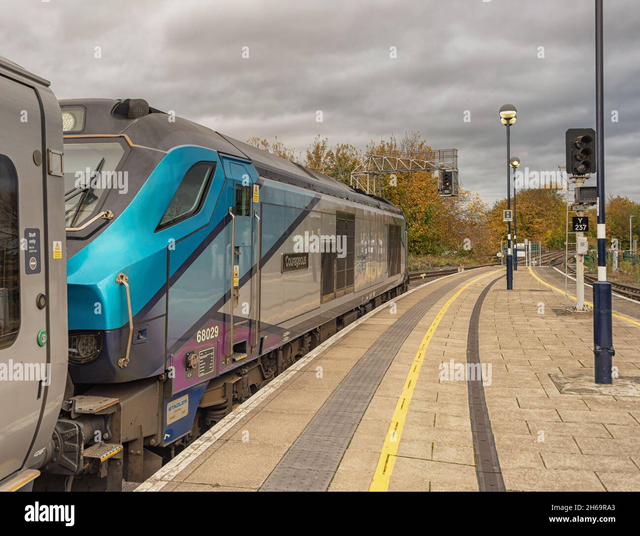 A modern locomotive stands at railway station platform with trees ...