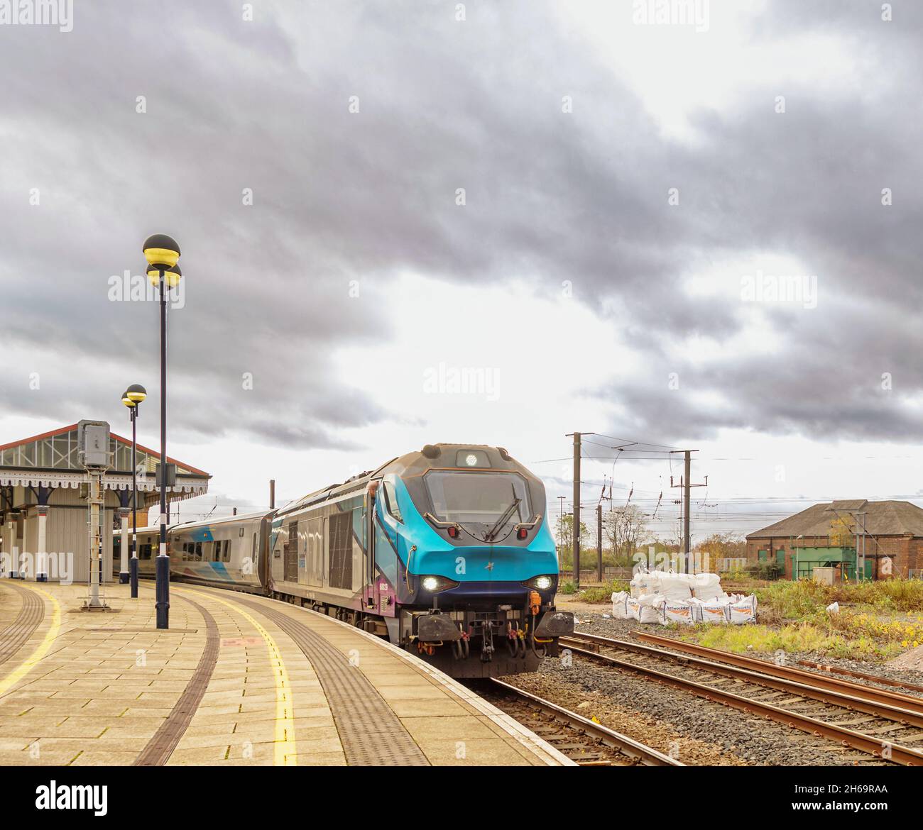 A modern locomotive stands at railway station platform with a historic ...