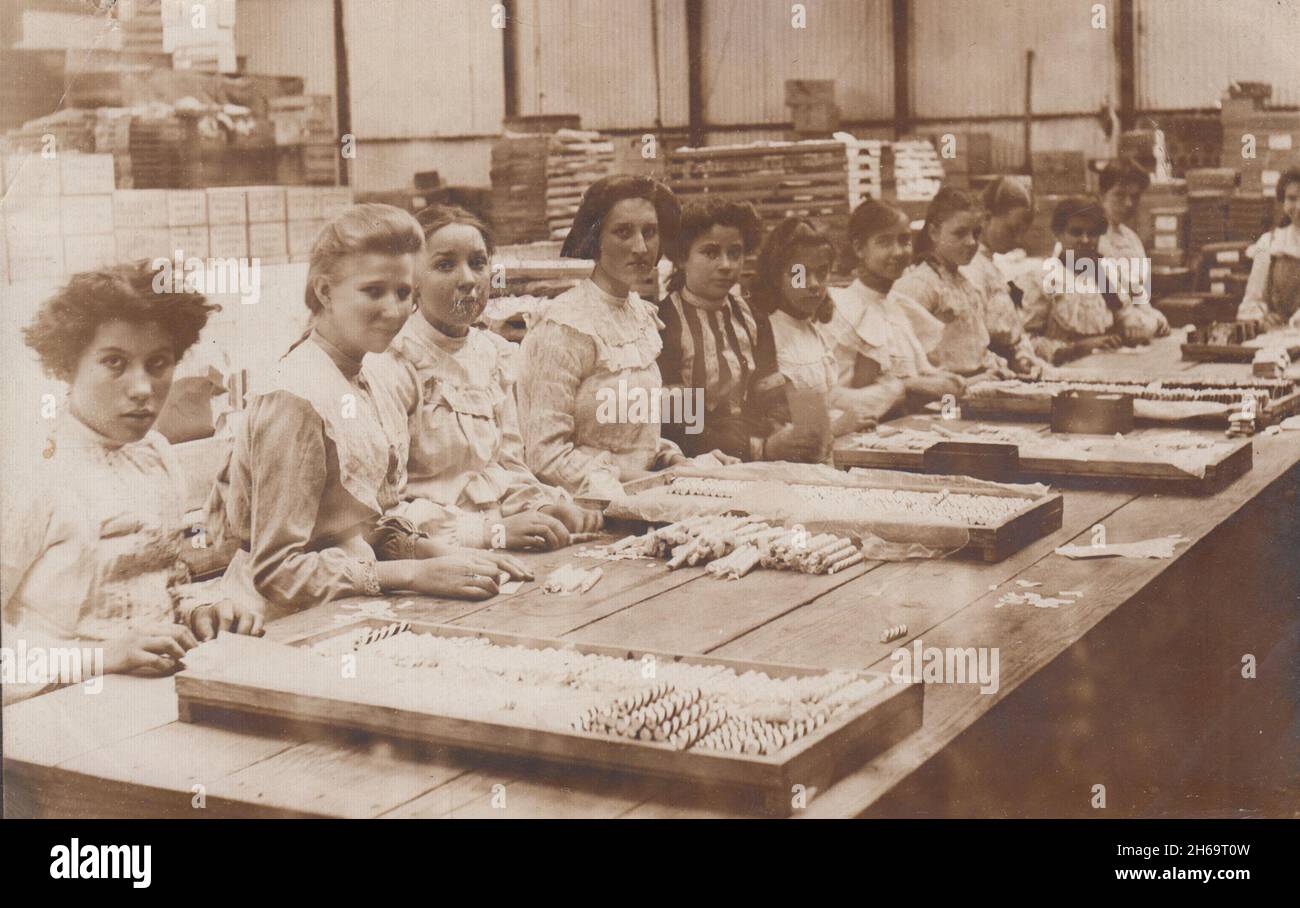 Women factory workers sat at benches making sweets, sticks of rock are ...