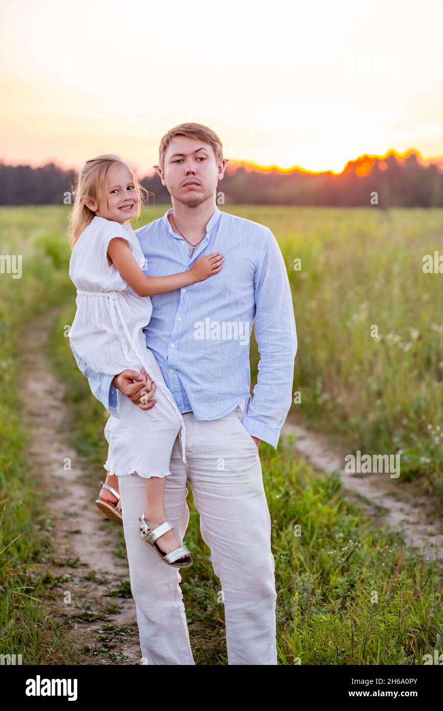 Little caucasian daughter in father's arms in the field on sunset ...