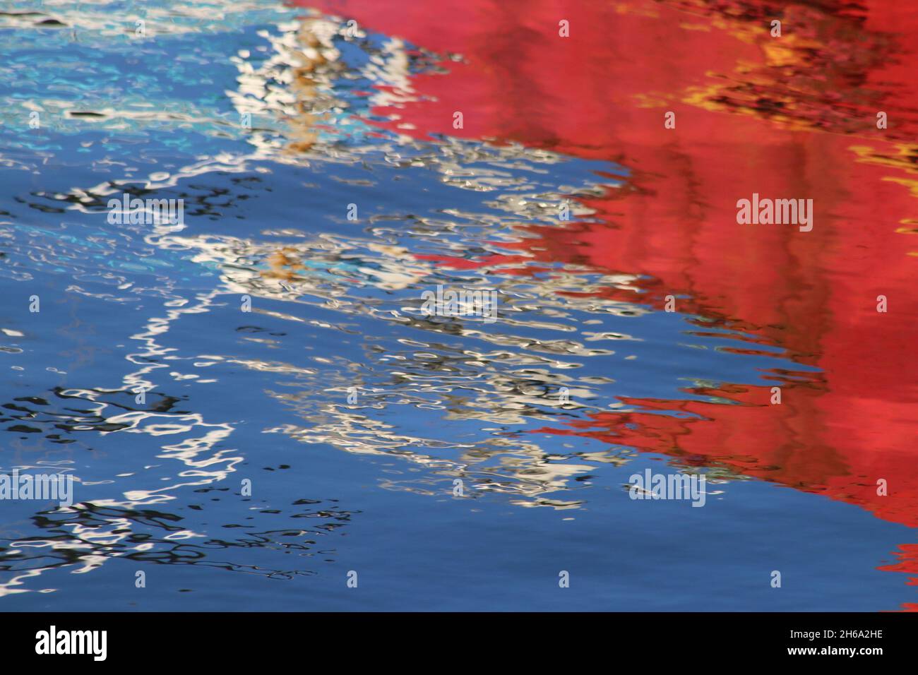Shapes and colours in reflections of fishing boats in water of harbour ...