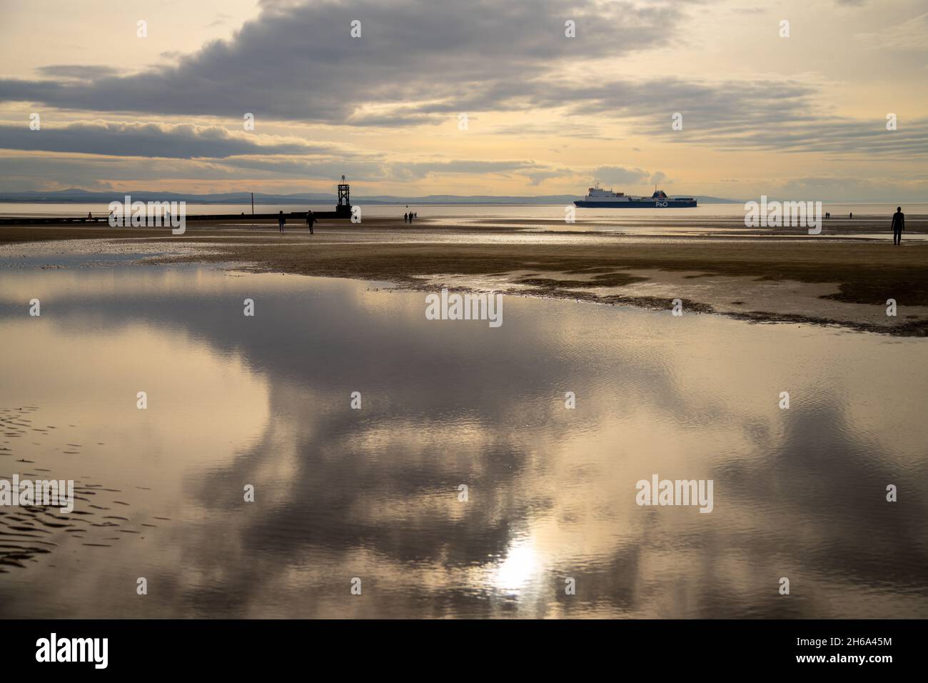 A Crosby beach at sunset with ferry boat sailing up Mersey estuary to ...