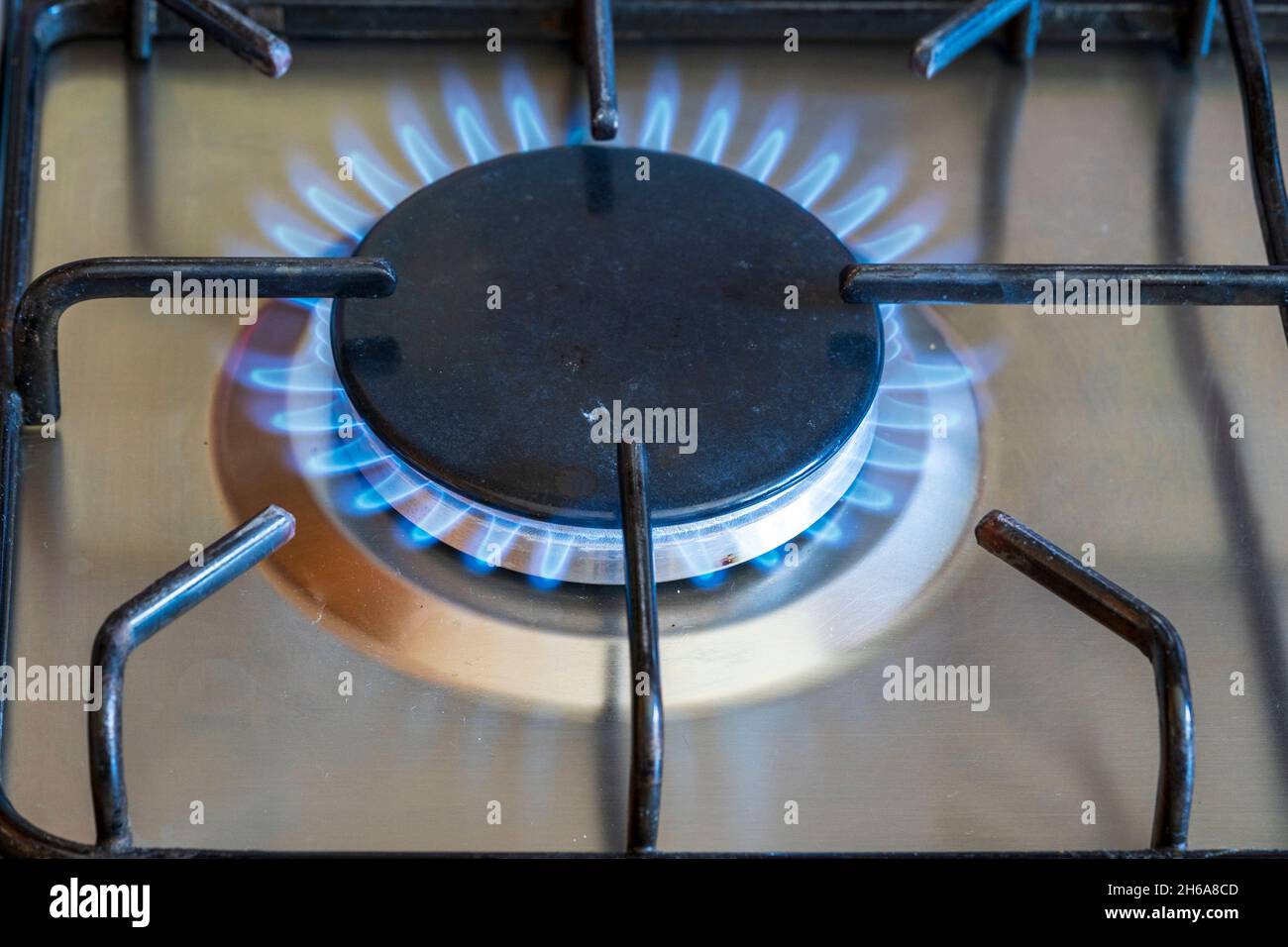 Gas ring alight on gas cooker hob. Circular grey ring topped with cast ...