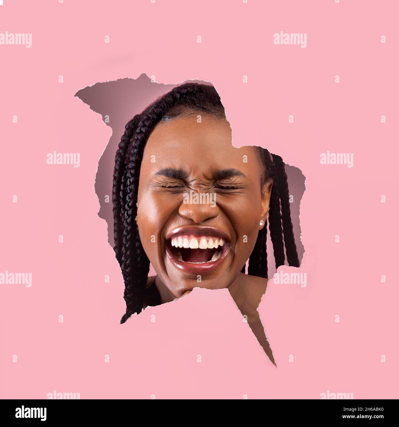 Closeup of female face breaking through hole in ripped pink paper ...