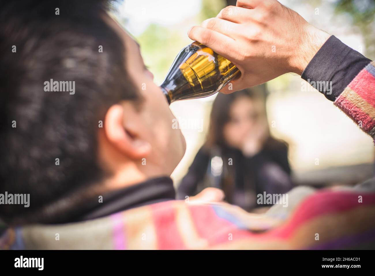Young couple chugging beer from bottle on wooden bench with table in ...