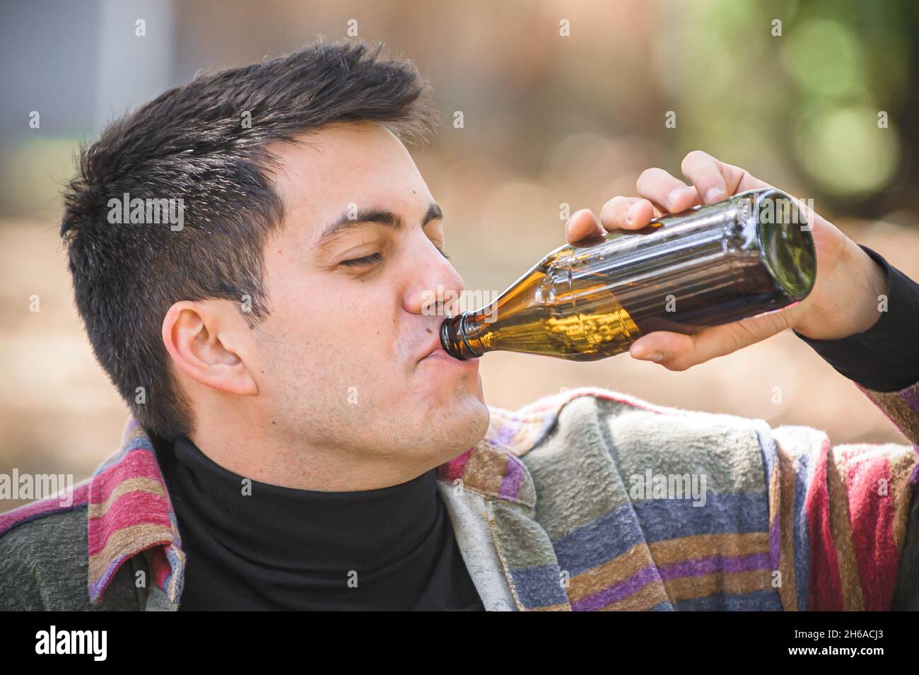 Man chug beer from bottle on wooden bench with table in forest park ...