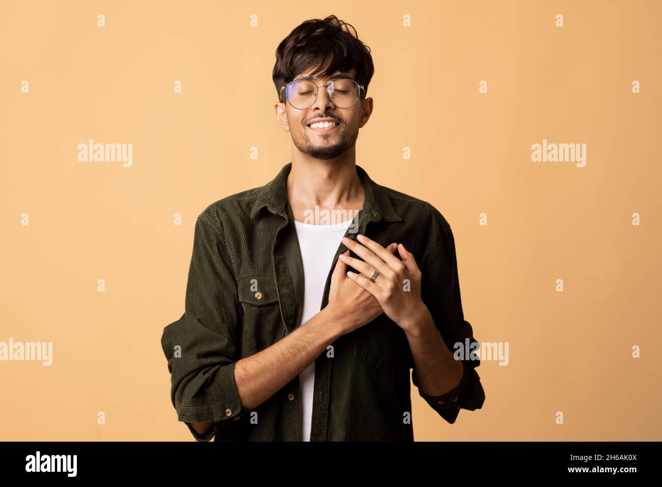 Peaceful hindu guy with closed eyes holding hands over heart, praying ...