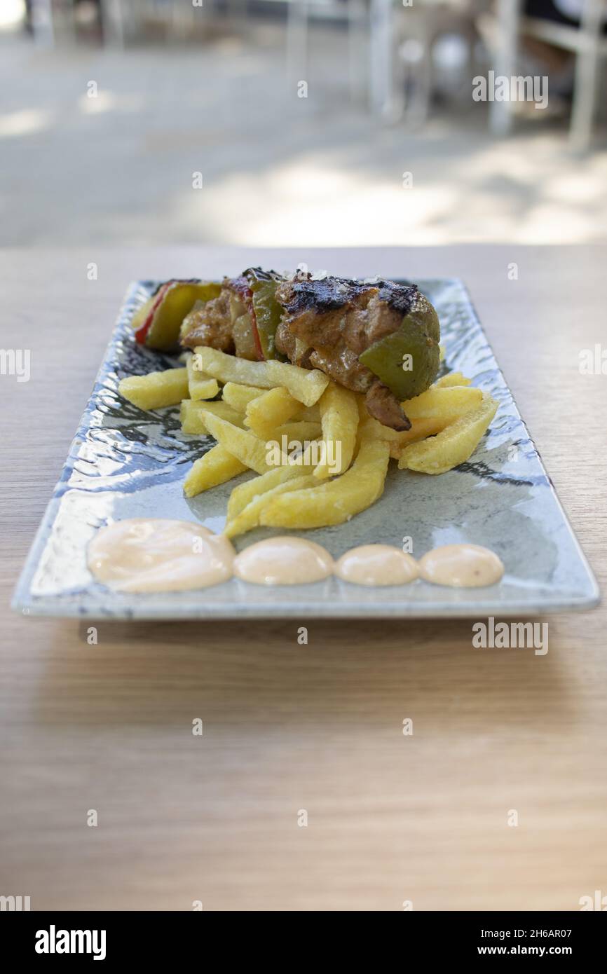 A vertical closeup of a Tapa lamb skewer dish with fries served in a ...