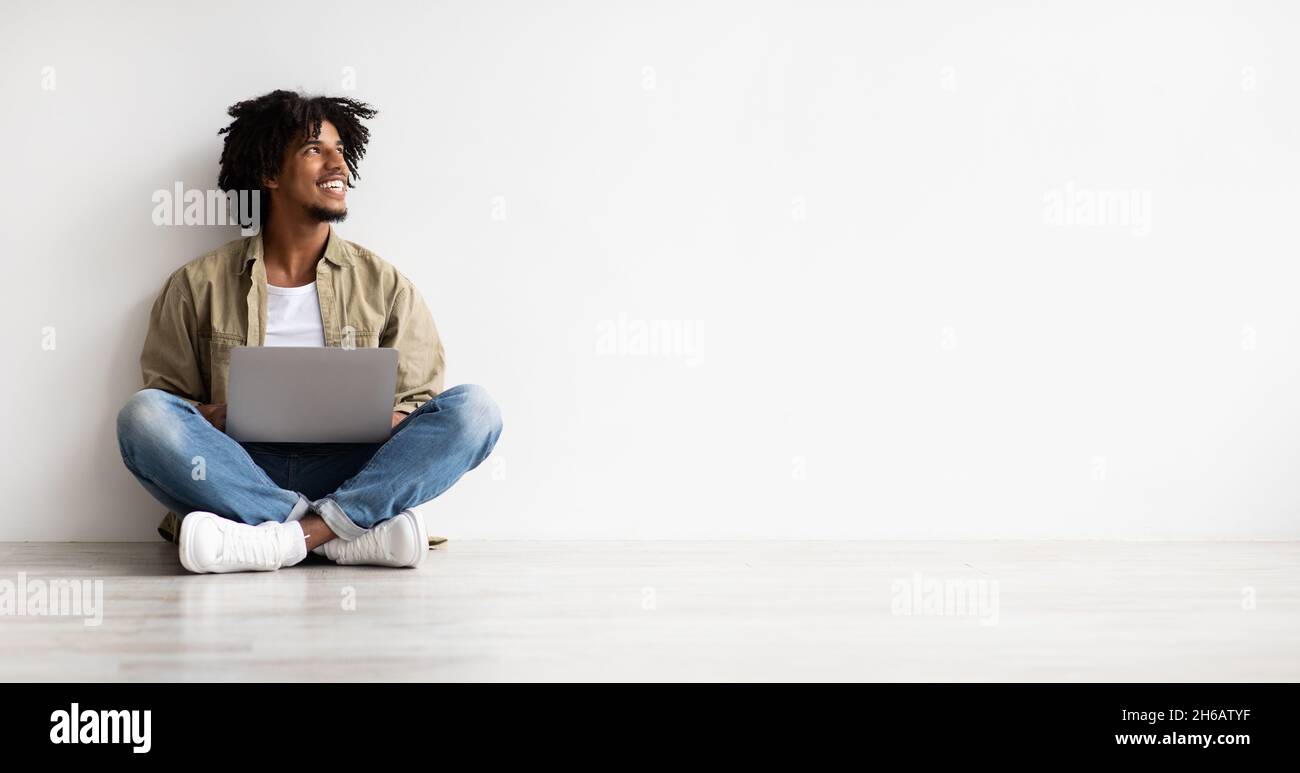 Young African American Man Sitting On Floor With Laptop And Looking ...