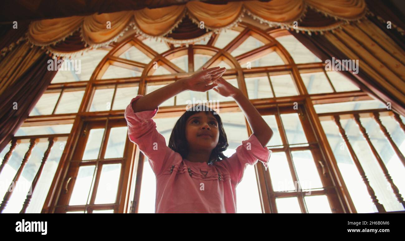 A low angle shot of a little Indian girl dancing next to the window ...