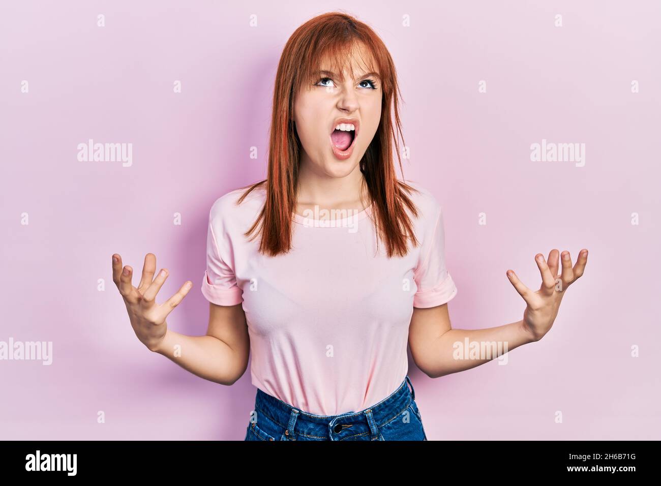 Redhead young woman wearing casual pink t shirt crazy and mad shouting ...