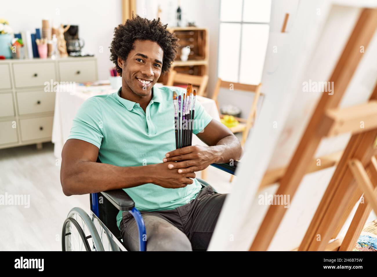 Young african american disabled artist man holding paintbrushes sitting ...