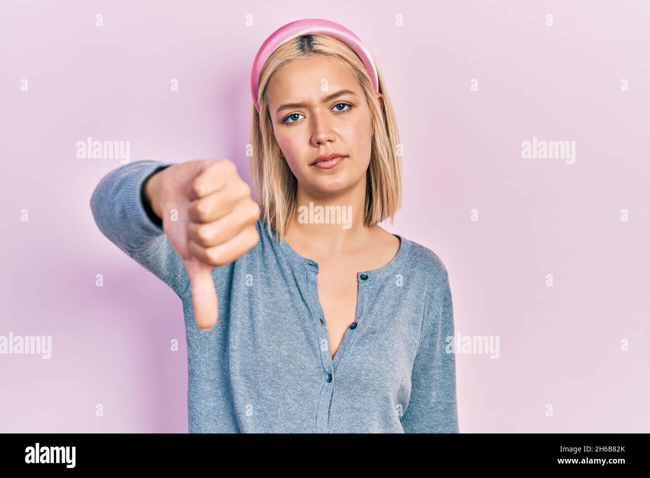 Beautiful blonde woman standing over pink background looking unhappy ...