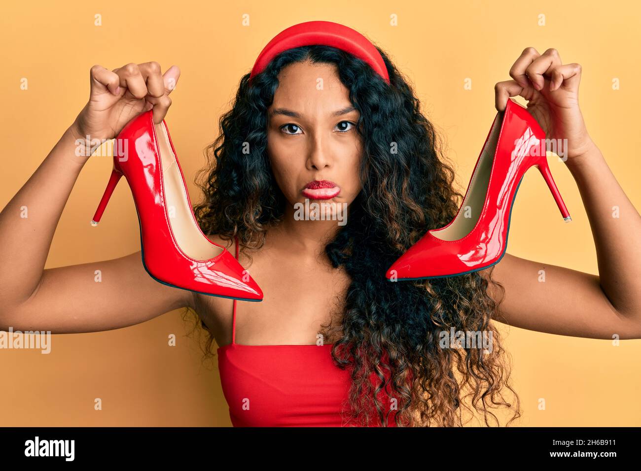 Young latin woman holding red high heel shoes depressed and worry for ...