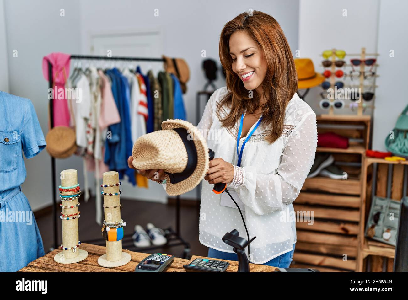 Young latin woman shopkeeper scanning hat using barcode reader at ...