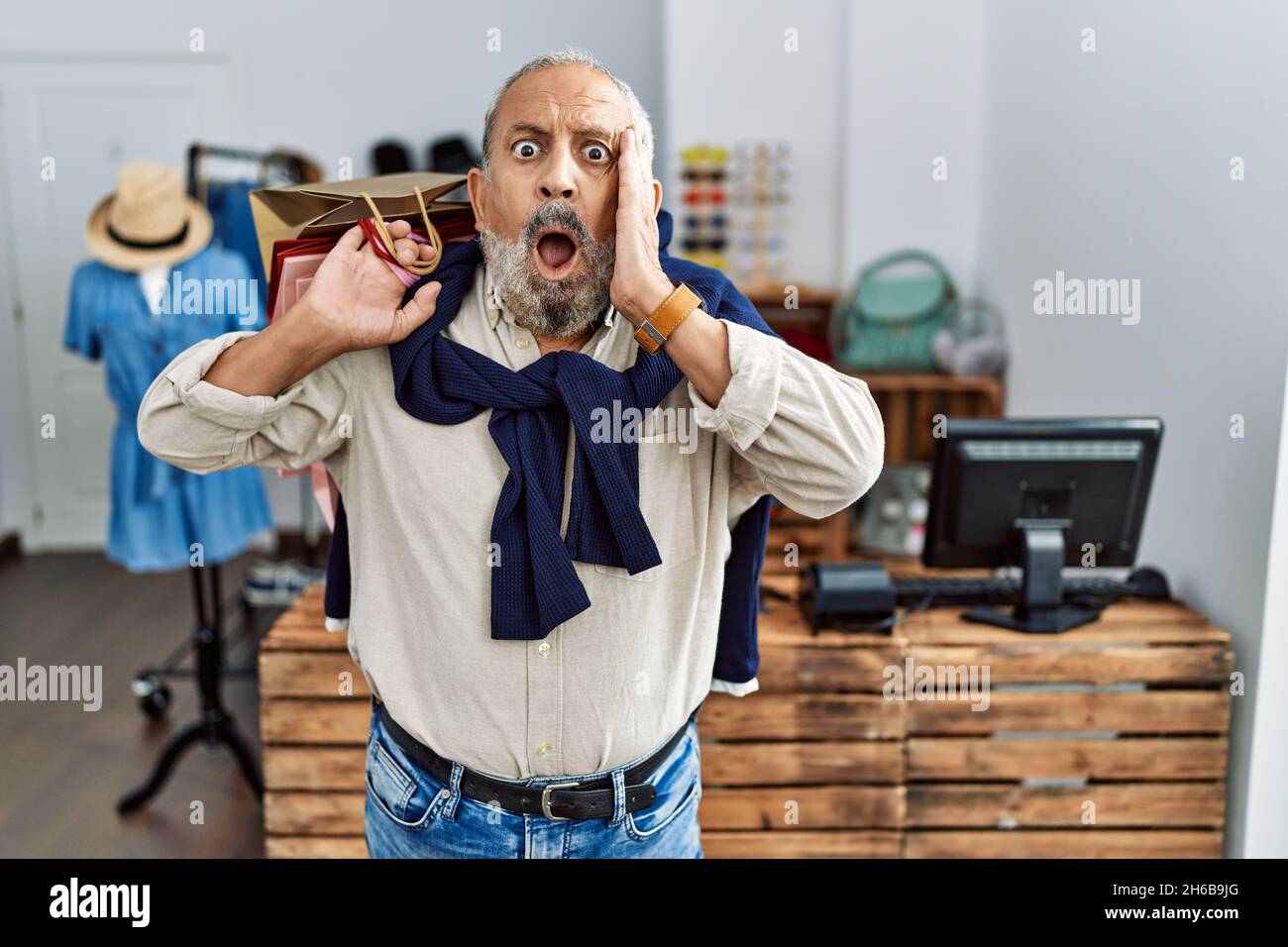 Handsome senior man holding shopping bags at boutique shop afraid and ...