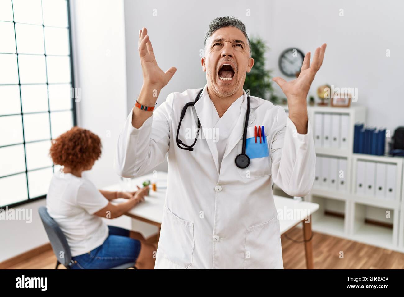 Middle age doctor man at the clinic with a patient crazy and mad ...