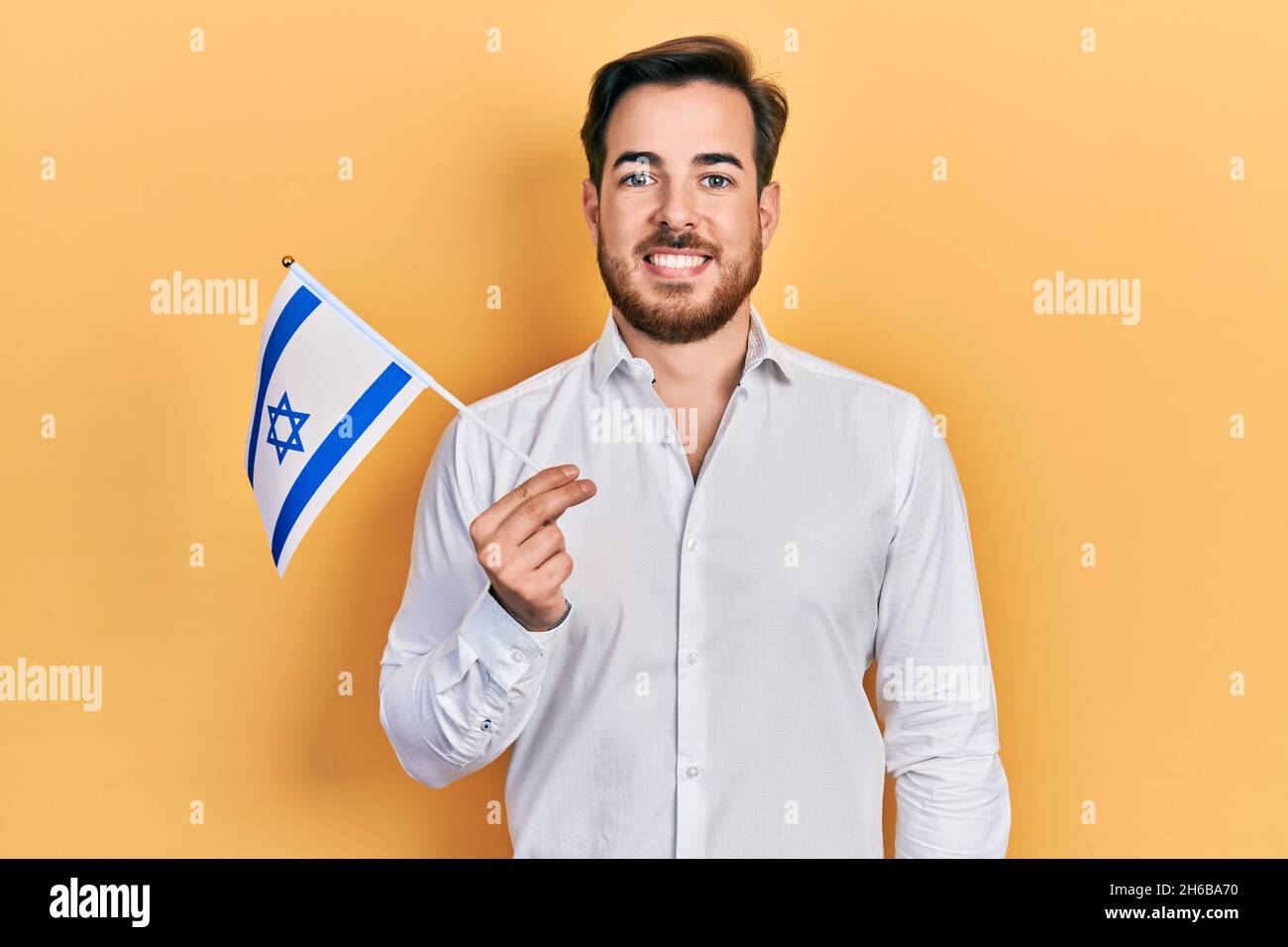 Handsome caucasian man with beard holding israel flag looking positive ...