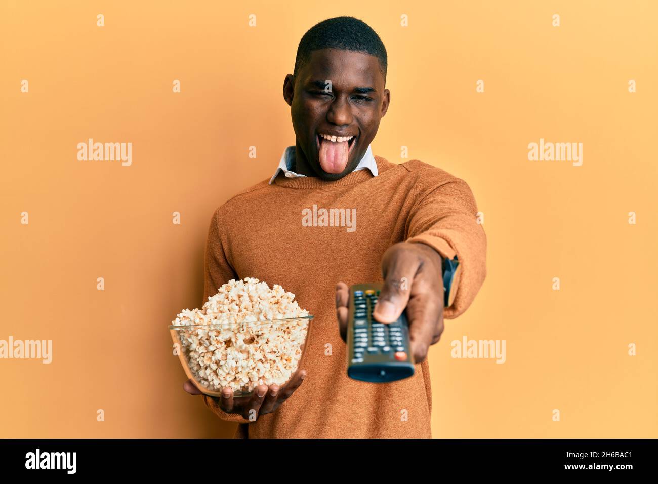 Young african american man holding television remote control eating ...