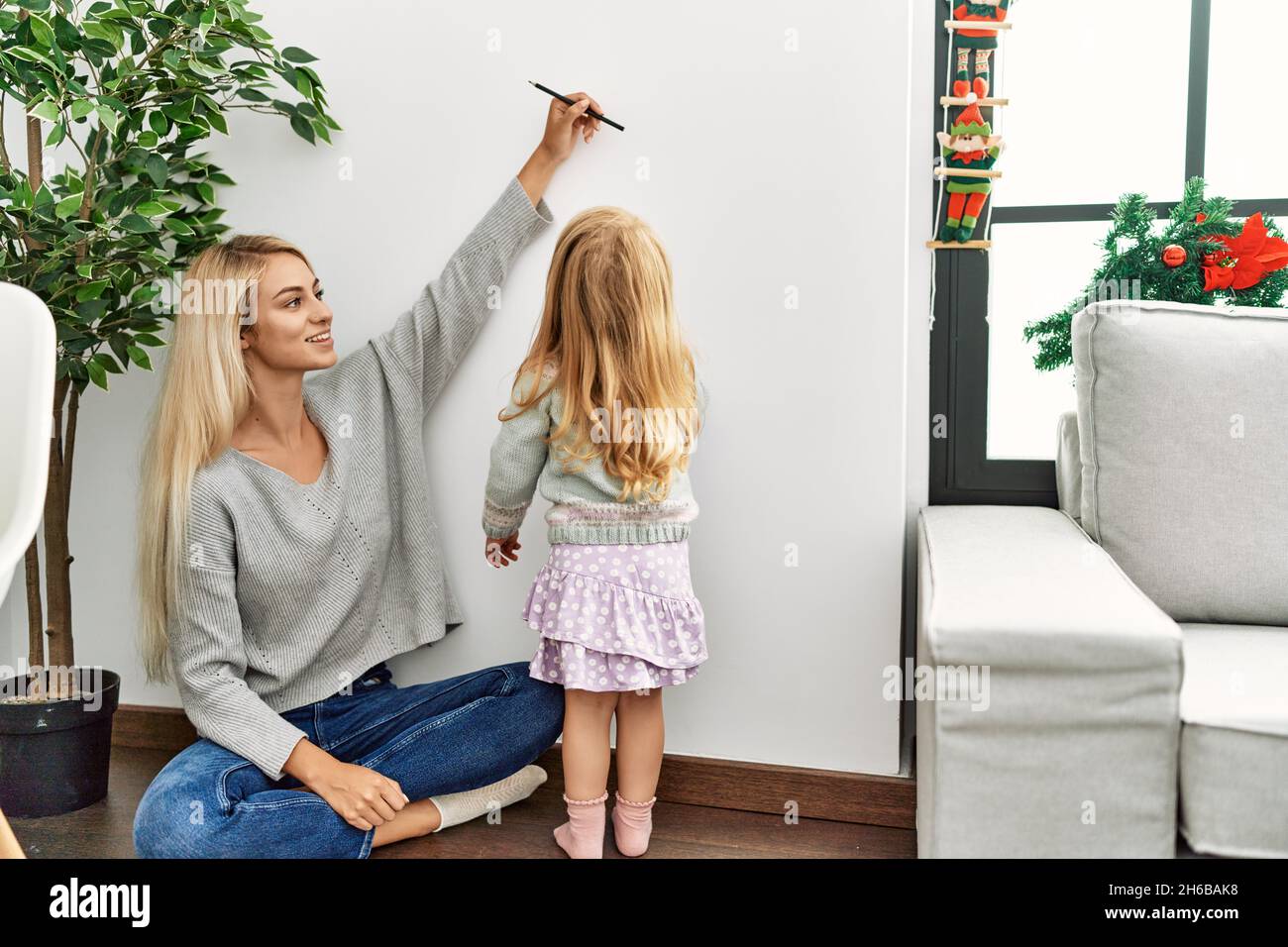 Mother and daughter measuring child height writing mark on wall at home ...