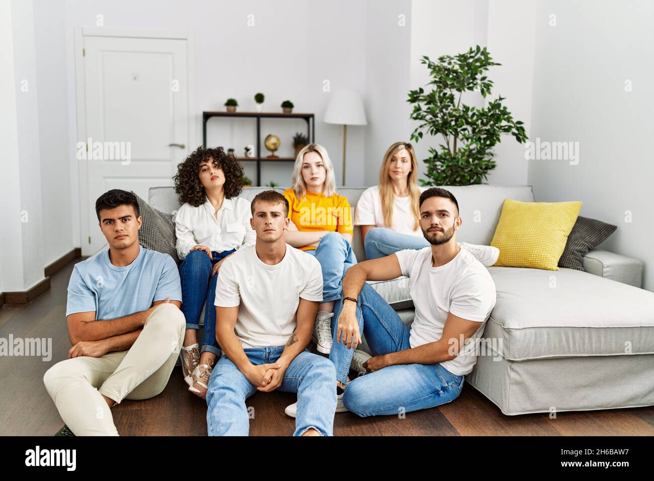 Group of people sitting on the sofa and floor at home with serious ...