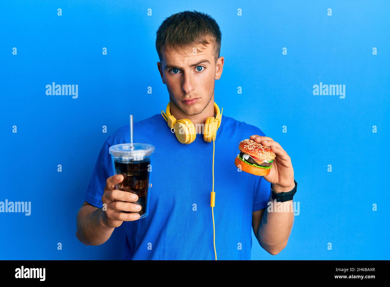 Young caucasian man eating a tasty classic burger and soda depressed ...