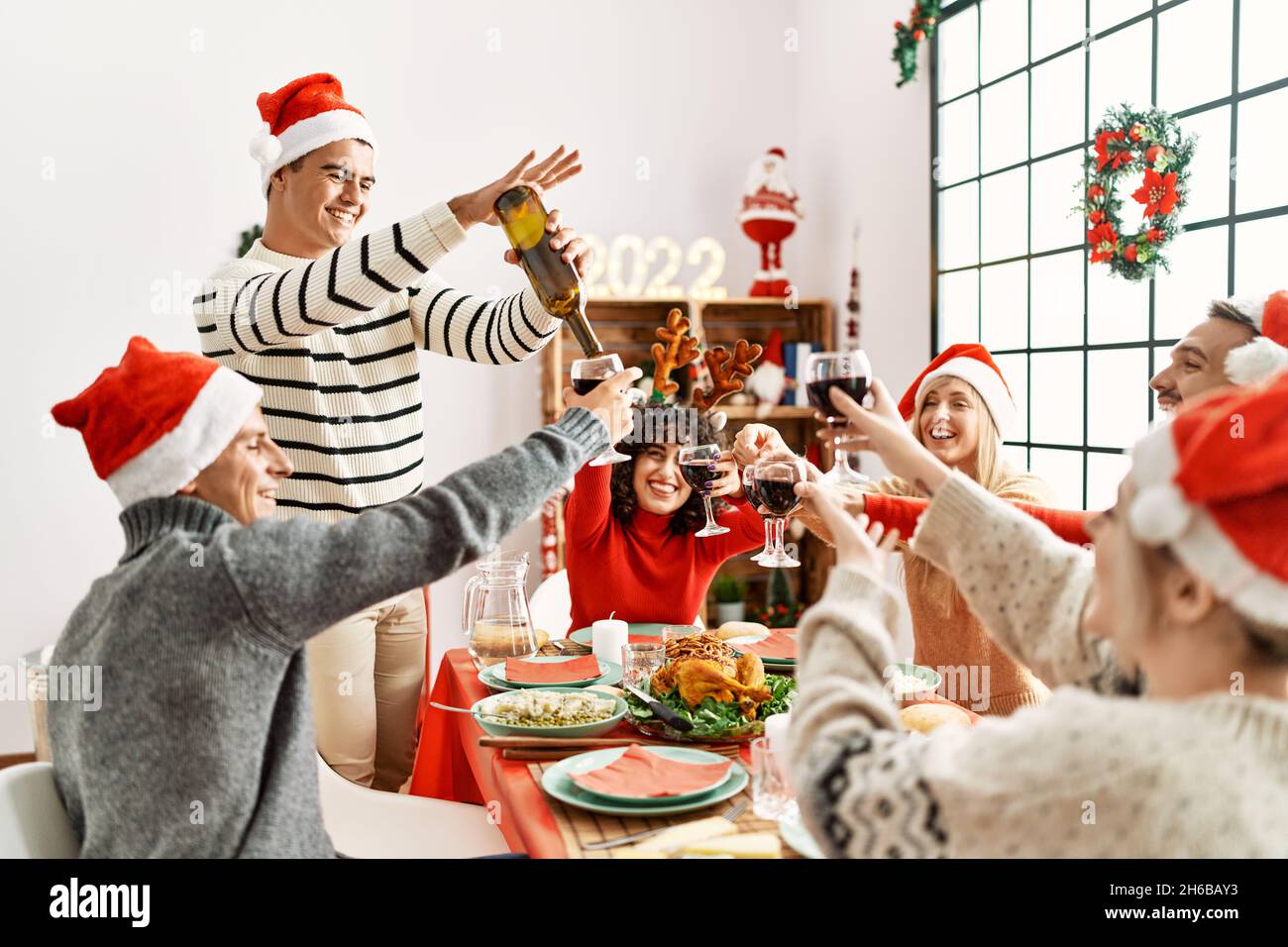 Group of young friends having christmas dinner pouring wine at home ...