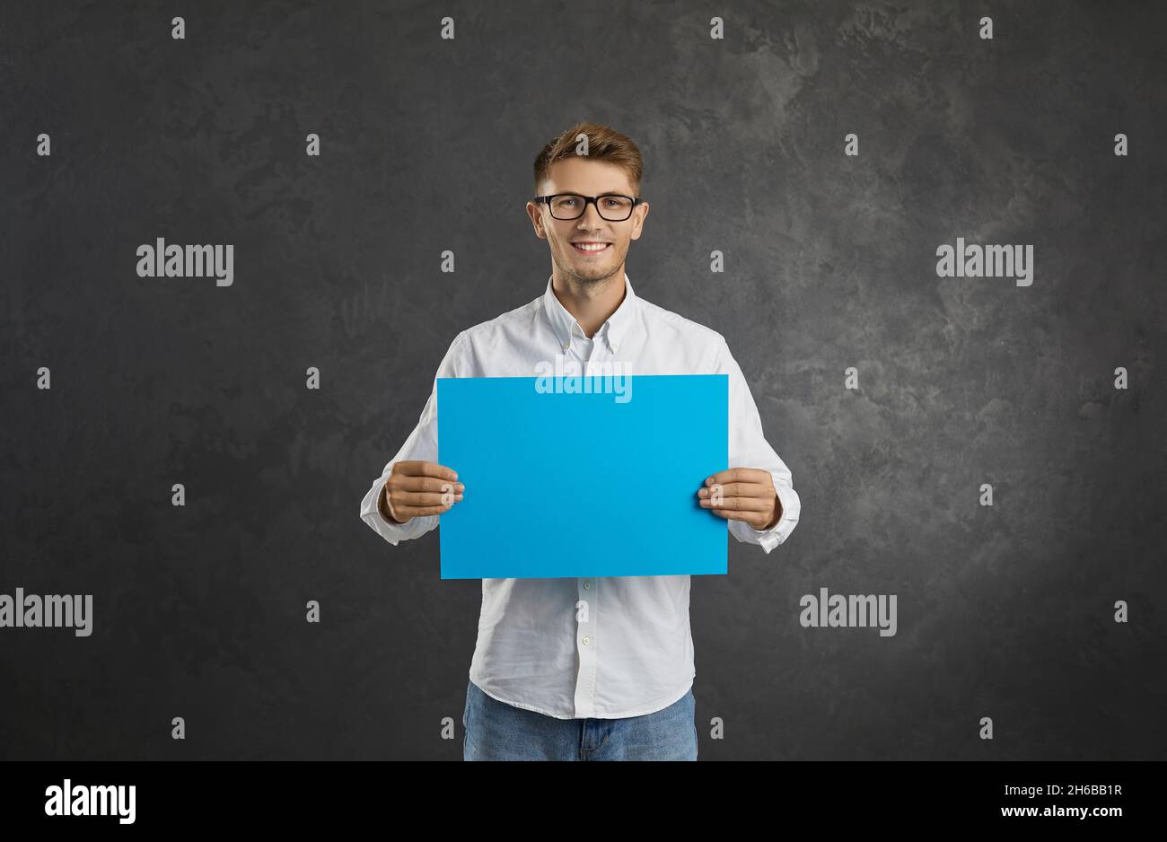 Portrait of a smiling young man showing a blank sheet of paper with ...