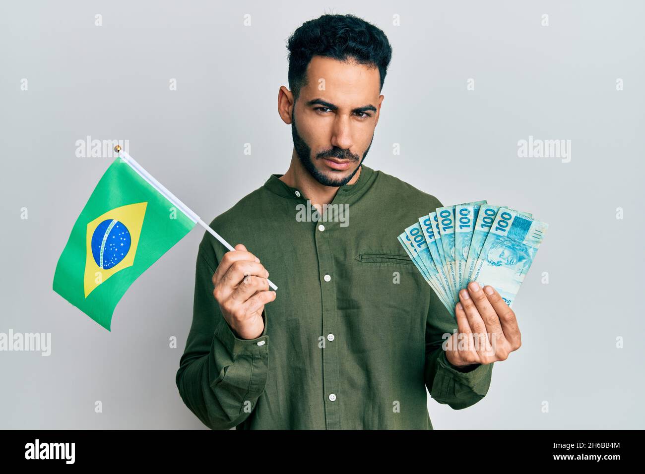 Young hispanic man holding brazil flag and real banknotes depressed and ...