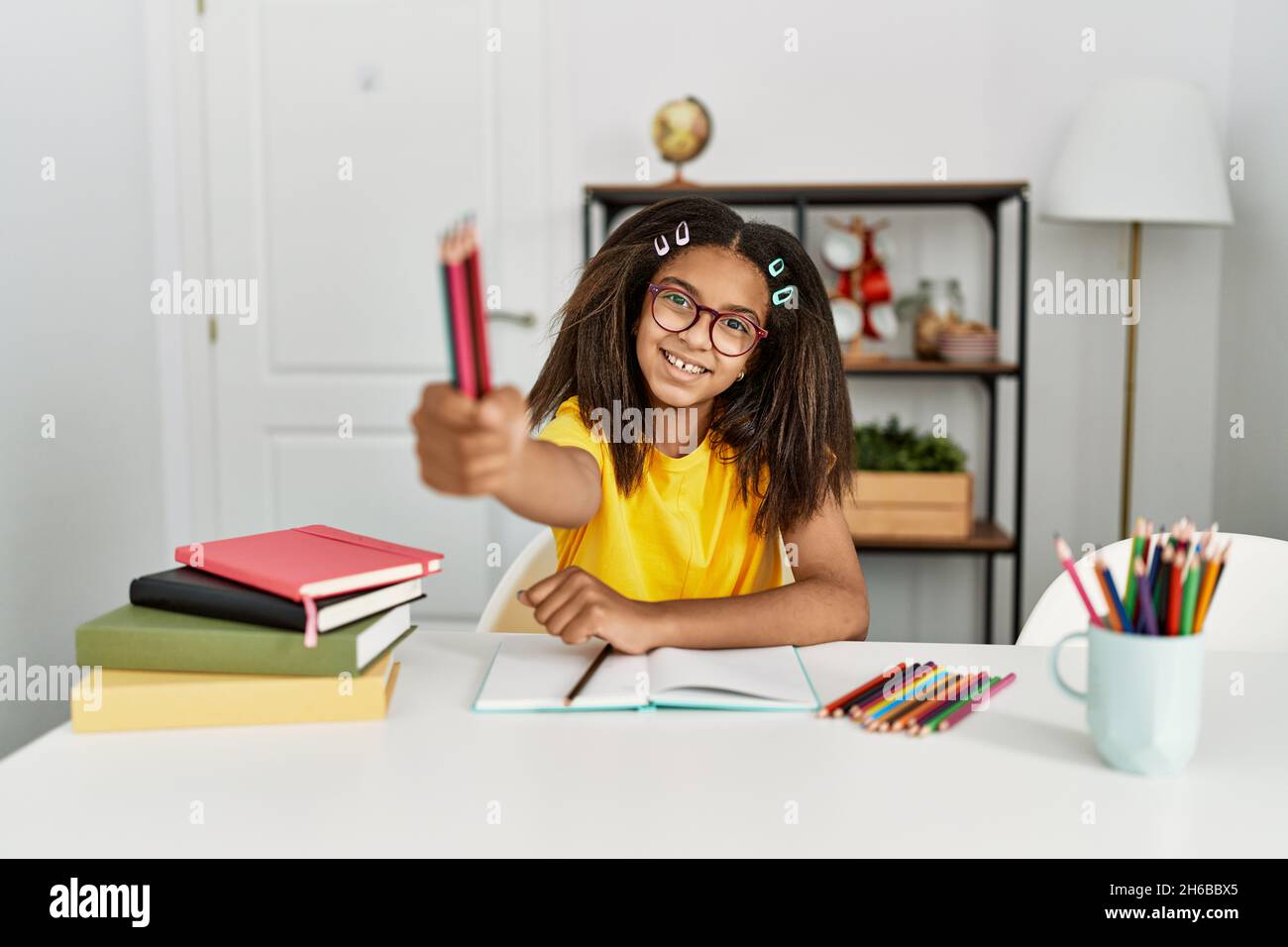 African american girl doing school homework holding pencils at home ...