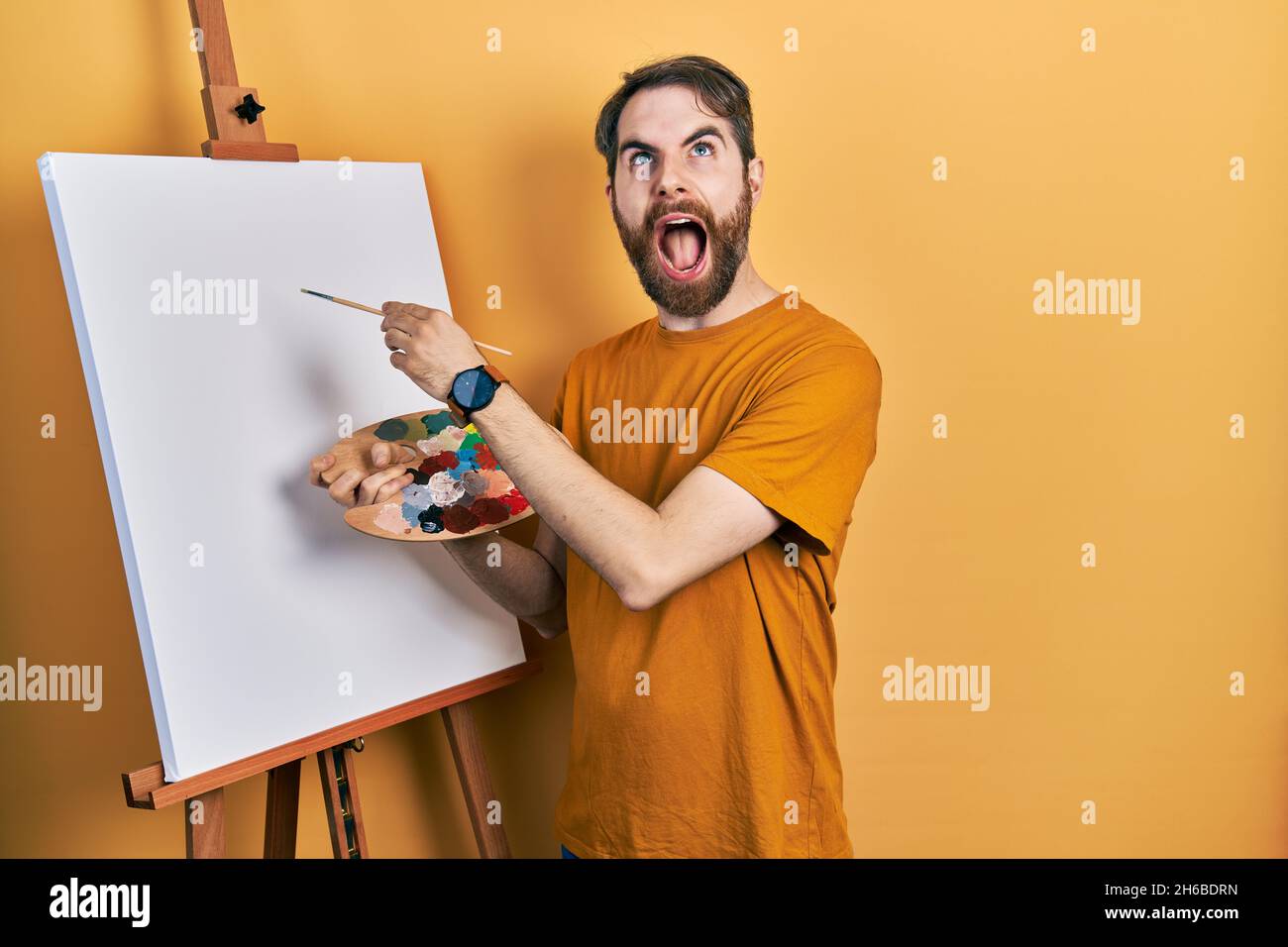 Caucasian man with beard standing drawing with palette by painter easel ...