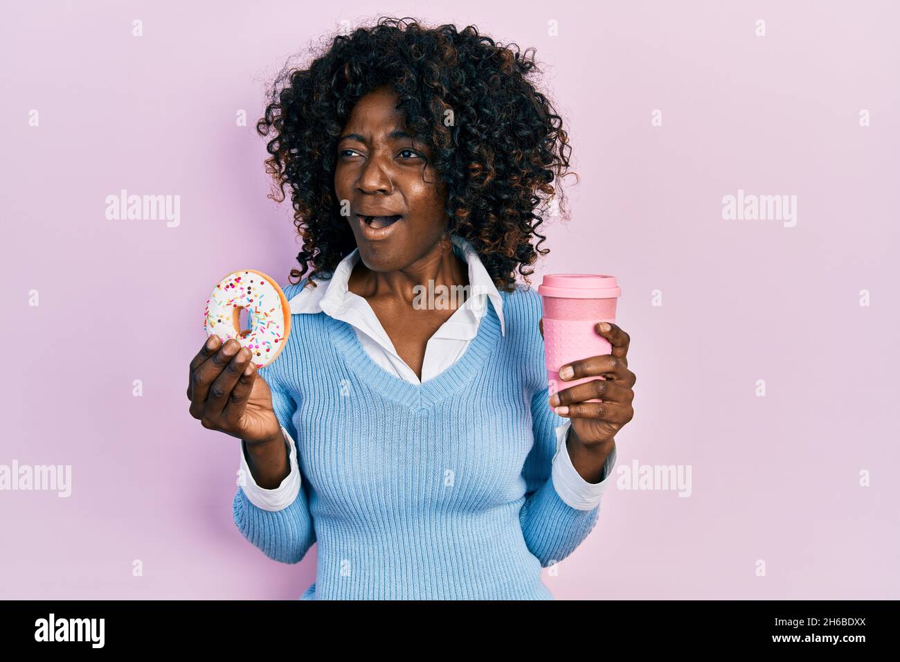Young african american woman eating doughnut and drinking coffee angry and mad screaming ...