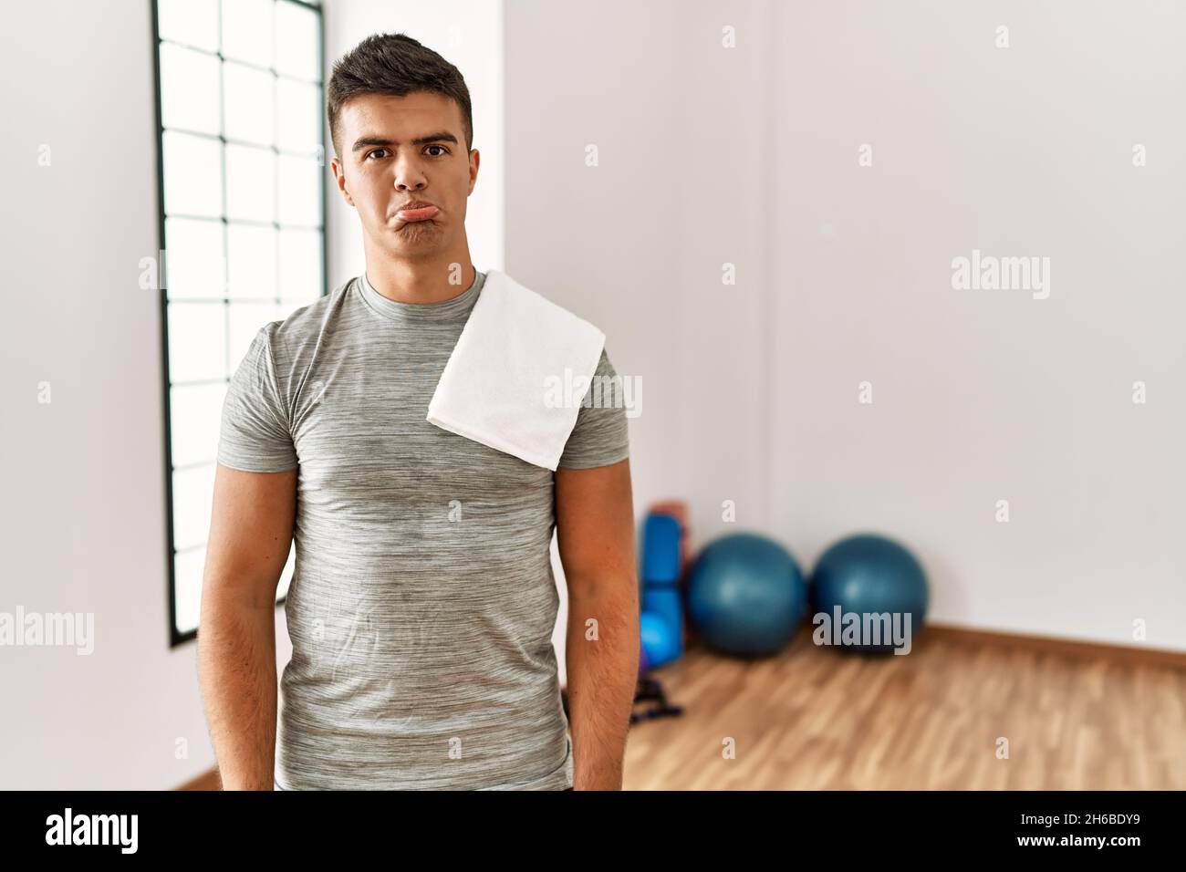 Young hispanic man wearing sportswear and towel at the gym depressed ...