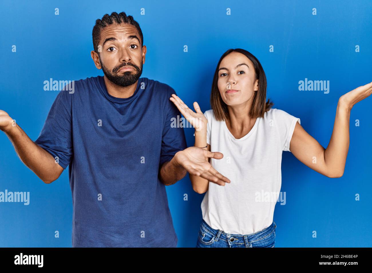 Young hispanic couple standing together clueless and confused ...